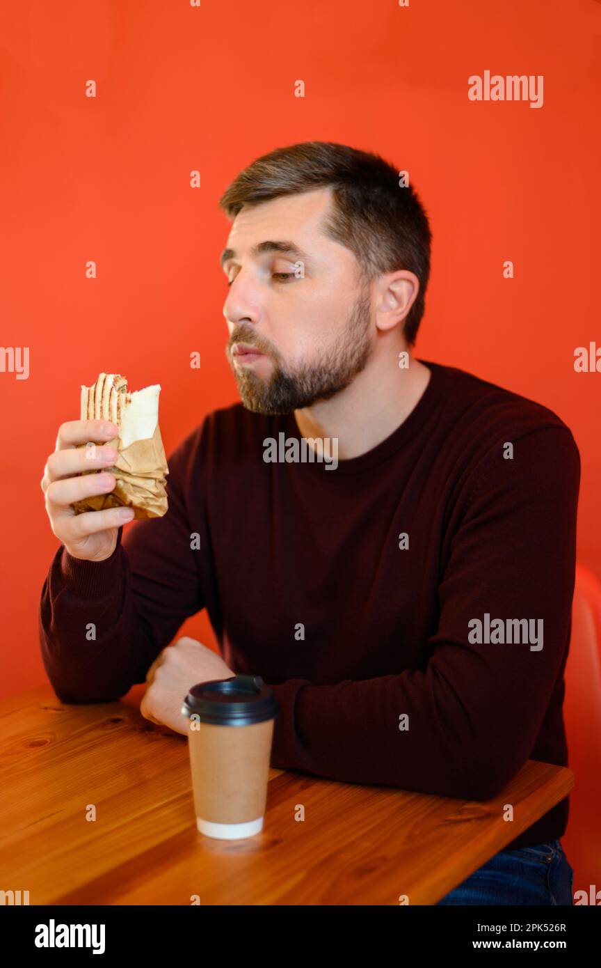 A man with a beard is sitting on a chair and eating shawarma, a quick ...