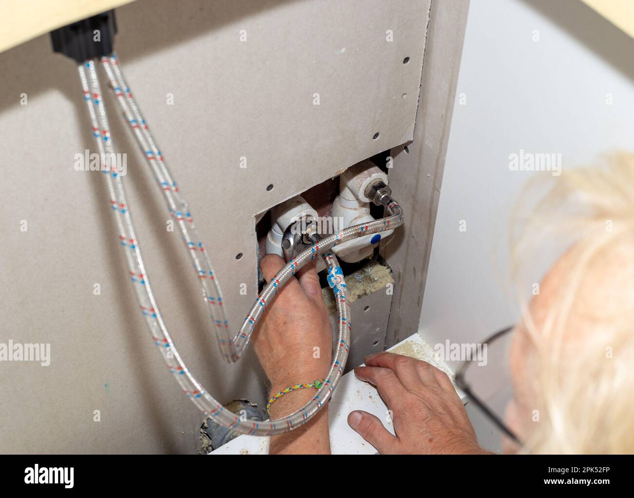A man installs a flexible hose to a water pipe in the kitchen ...