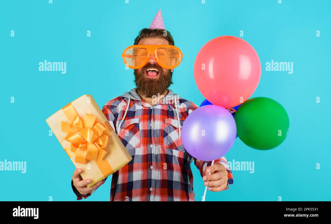 Bearded man in big glasses and party cap with present box and balloons ...