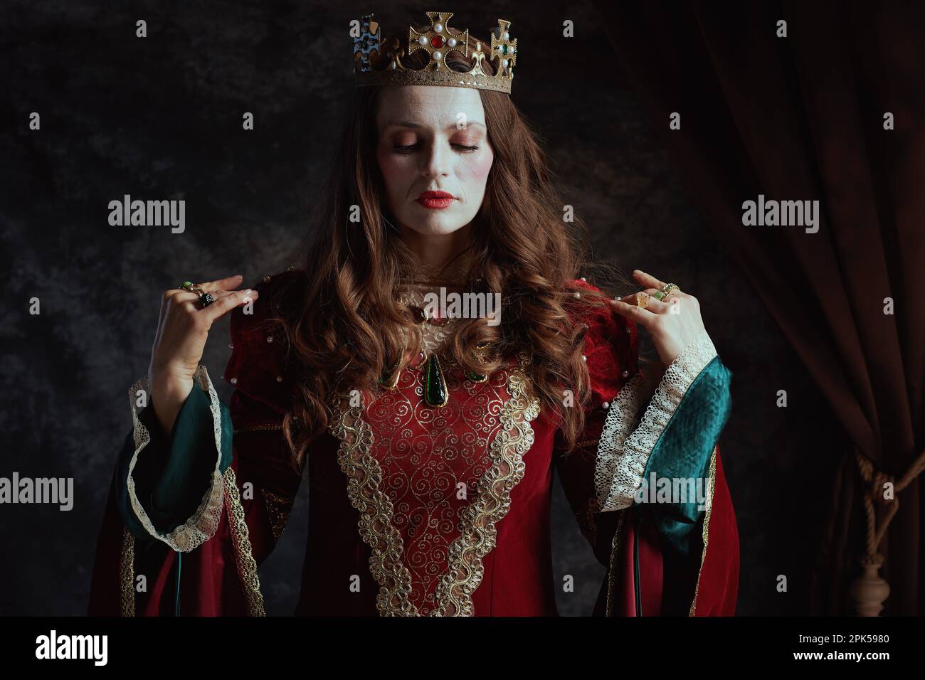 medieval queen in red dress with white makeup and crown on dark gray ...