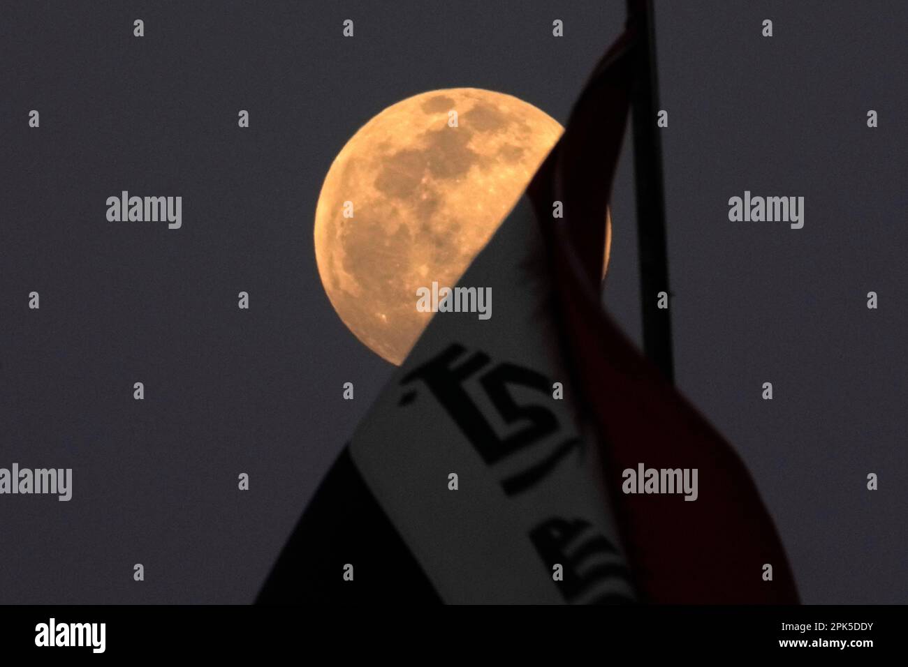 The moon rises over the Iraqi flag in the center of Baghdad, Iraq ...
