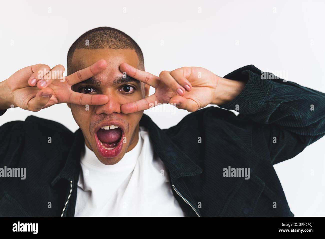 Crazy funny young adult man doing v sign in front of his face with both ...