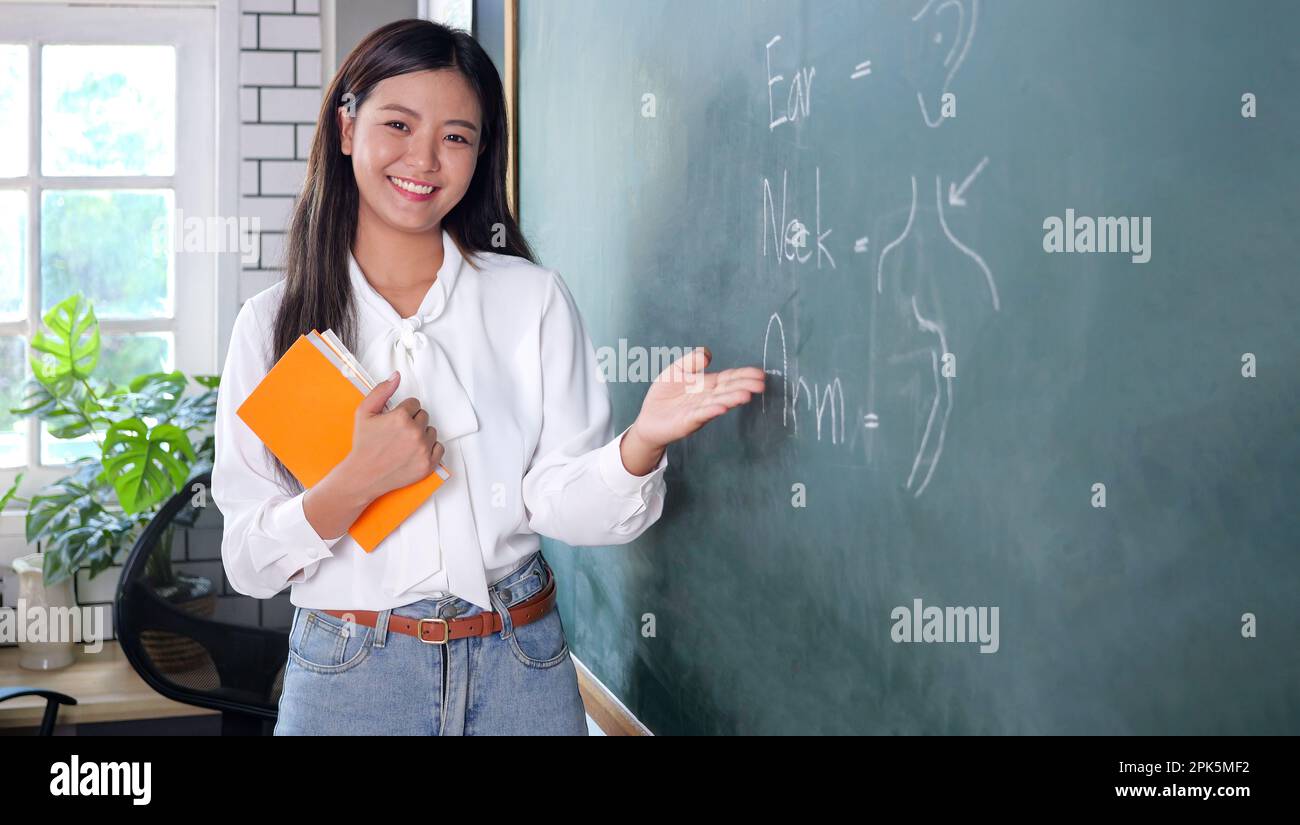 Teacher standing near backboard holding textbook posing to camera with ...
