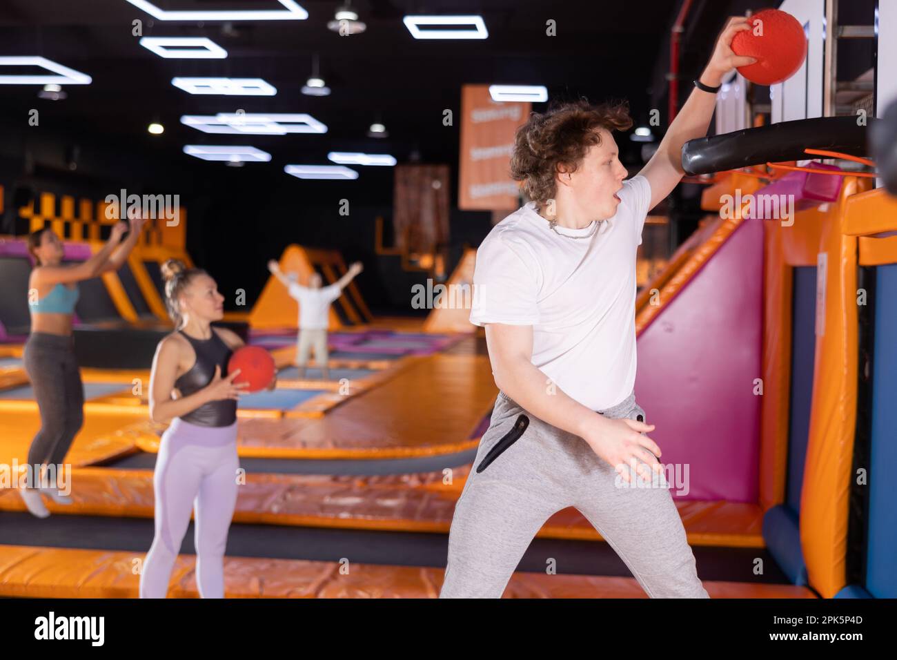 Teenage boy throwing ball in basket high jumping in trampoline arena ...