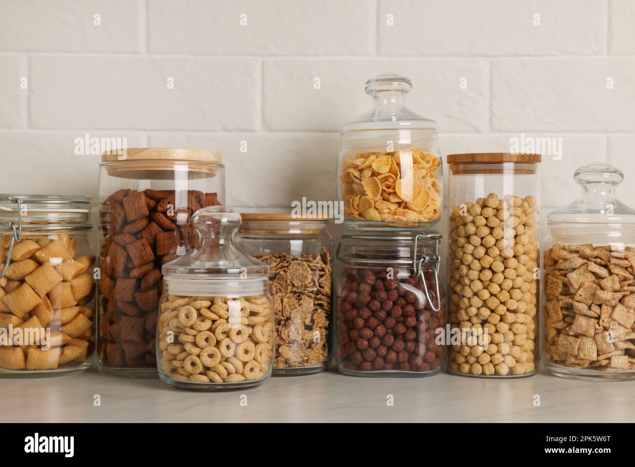 Glass containers with different breakfast cereals on white countertop ...