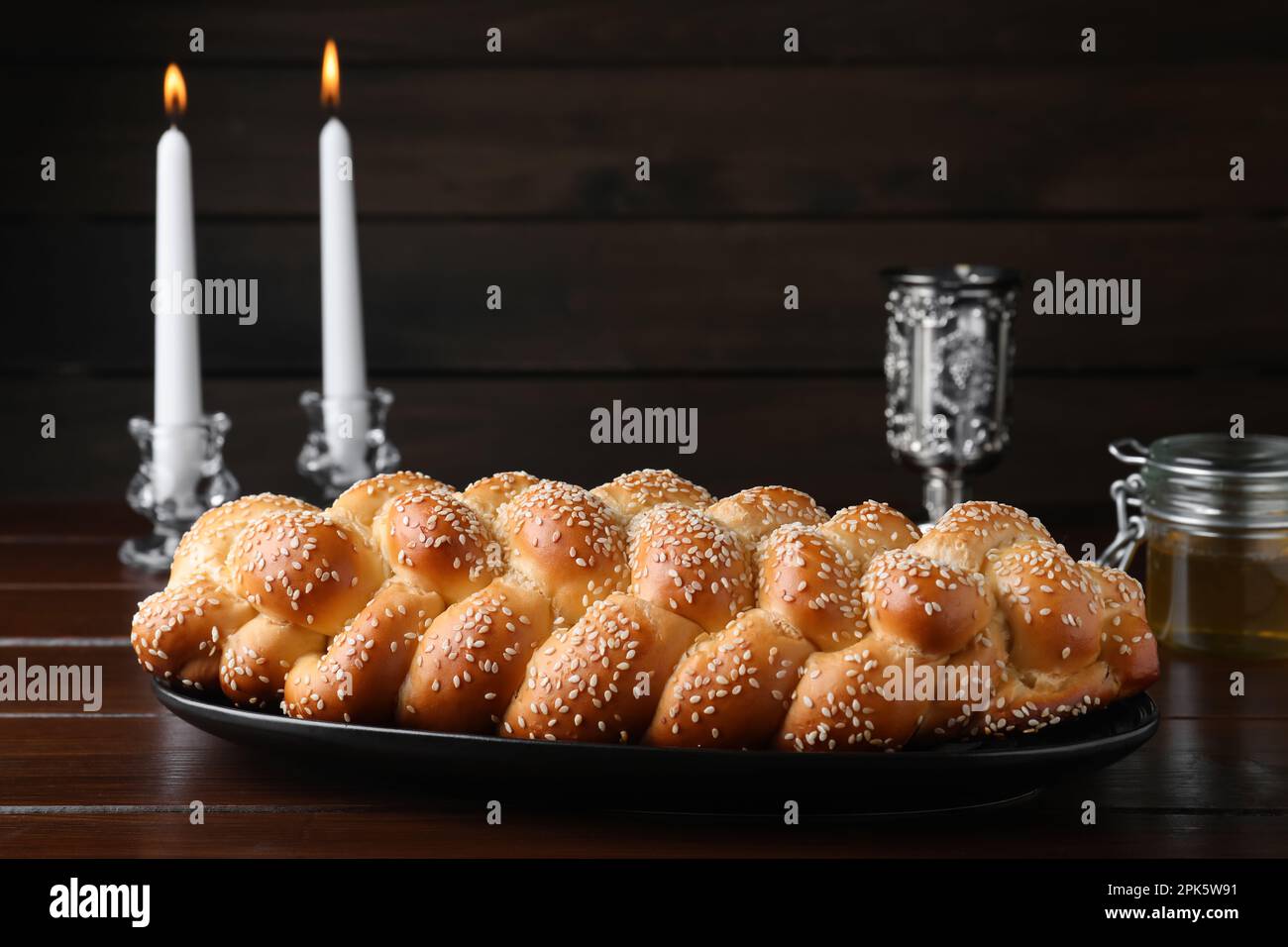 Homemade braided bread with sesame seeds, goblet and candles on wooden ...