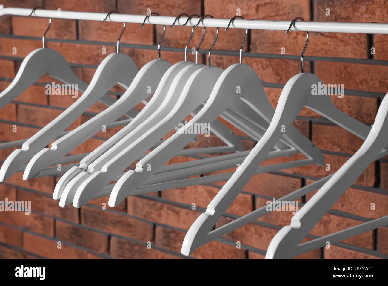 White clothes hangers on rail near red brick wall Stock Photo - Alamy