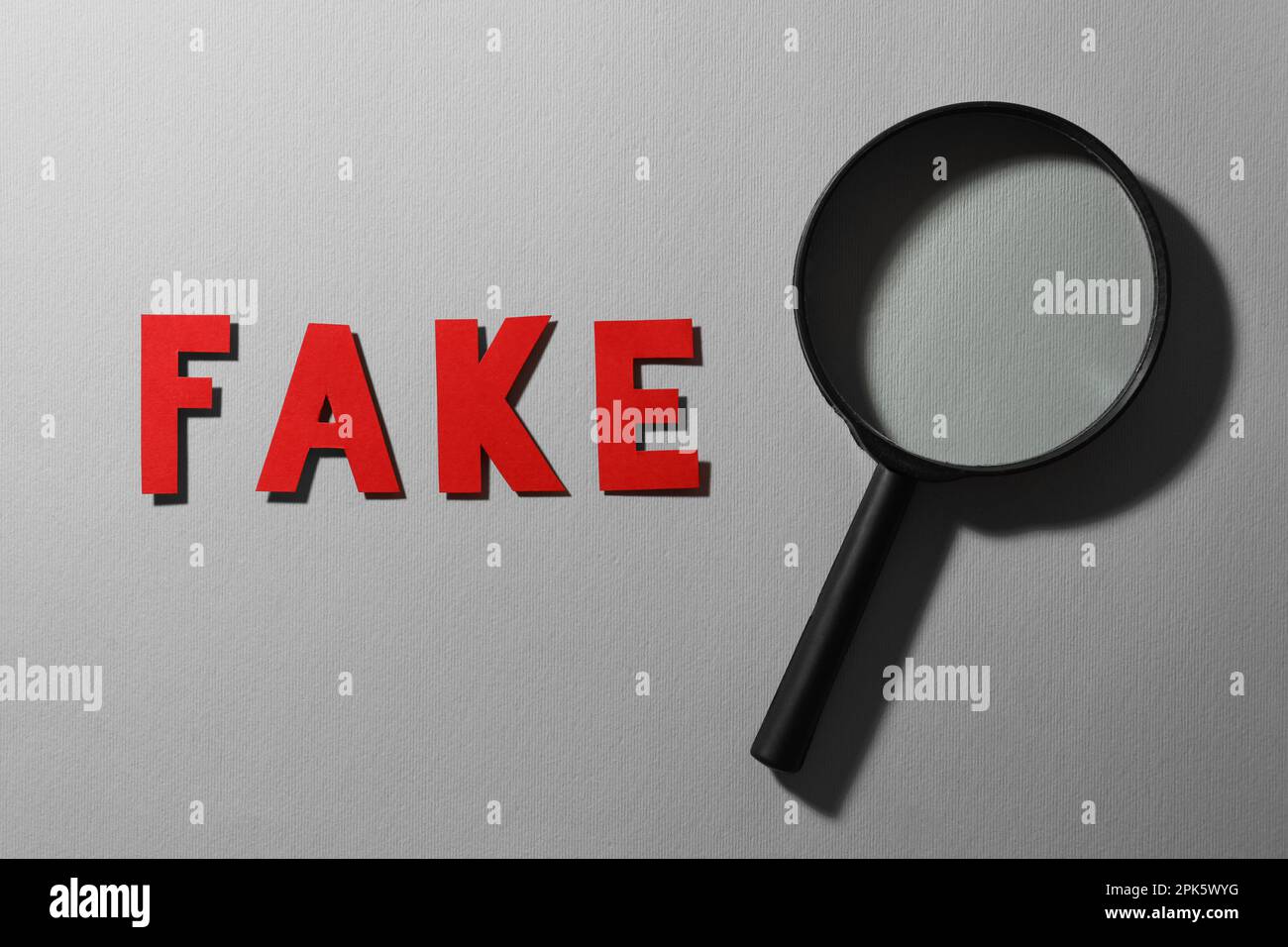 Word Fake made of red letters and magnifying glass on grey background ...
