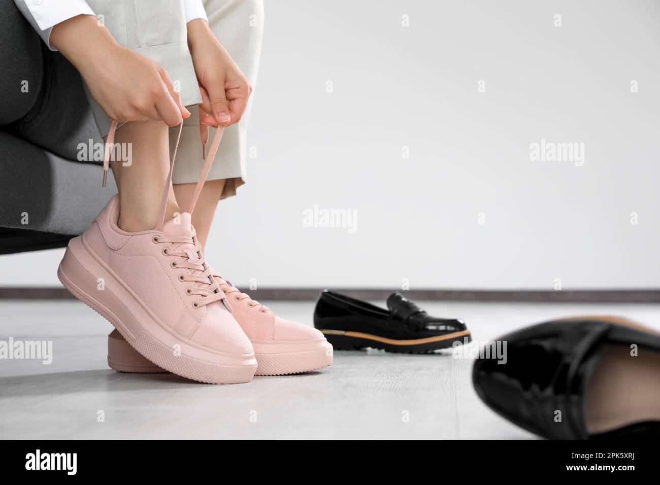 Woman taking off uncomfortable shoes and putting on sneakers in office ...