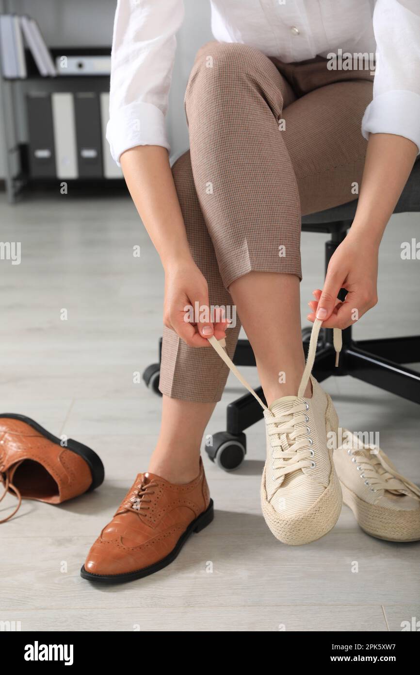Woman taking off uncomfortable shoes and putting on sneakers in office ...