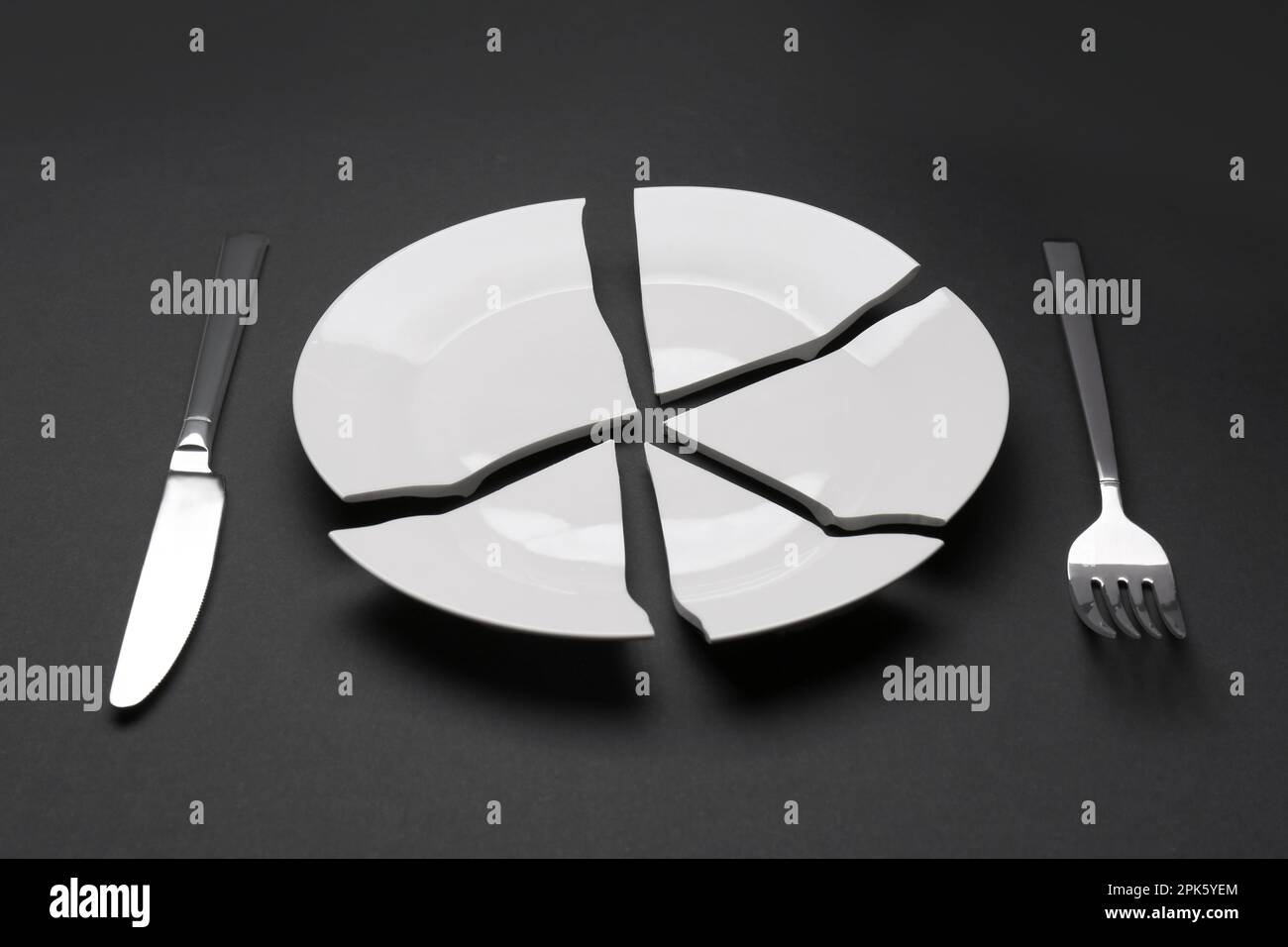 Pieces of broken ceramic plate and cutlery on dark grey background ...