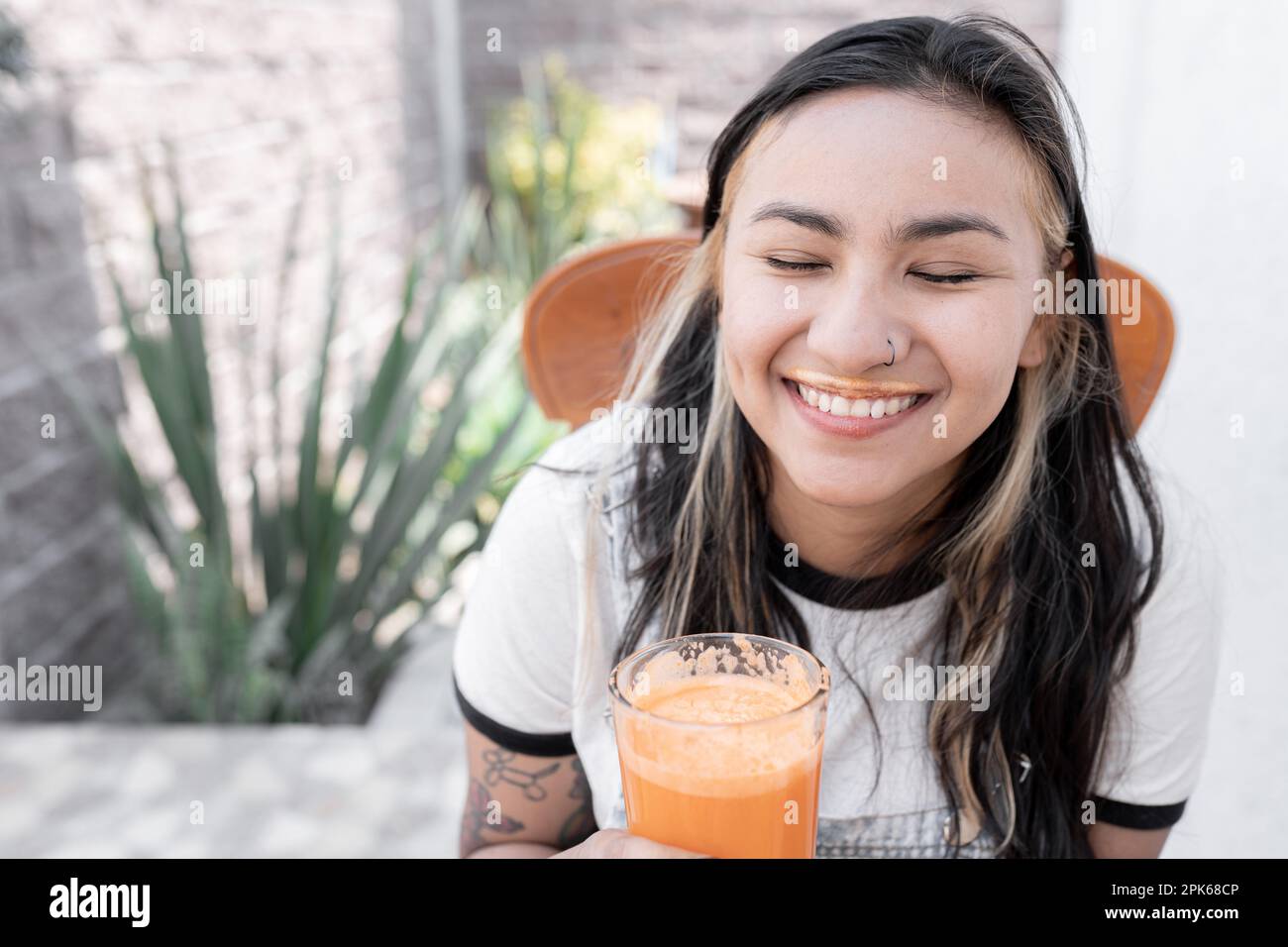 A young Hispanic woman is smiling with a foam moustache after drinking ...