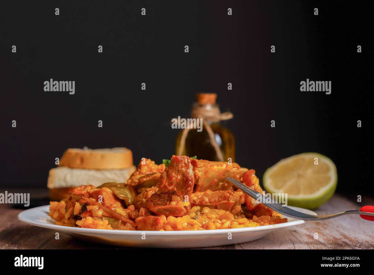 Plate of paella with ribs and green beans, with bread, lemon and bottle ...