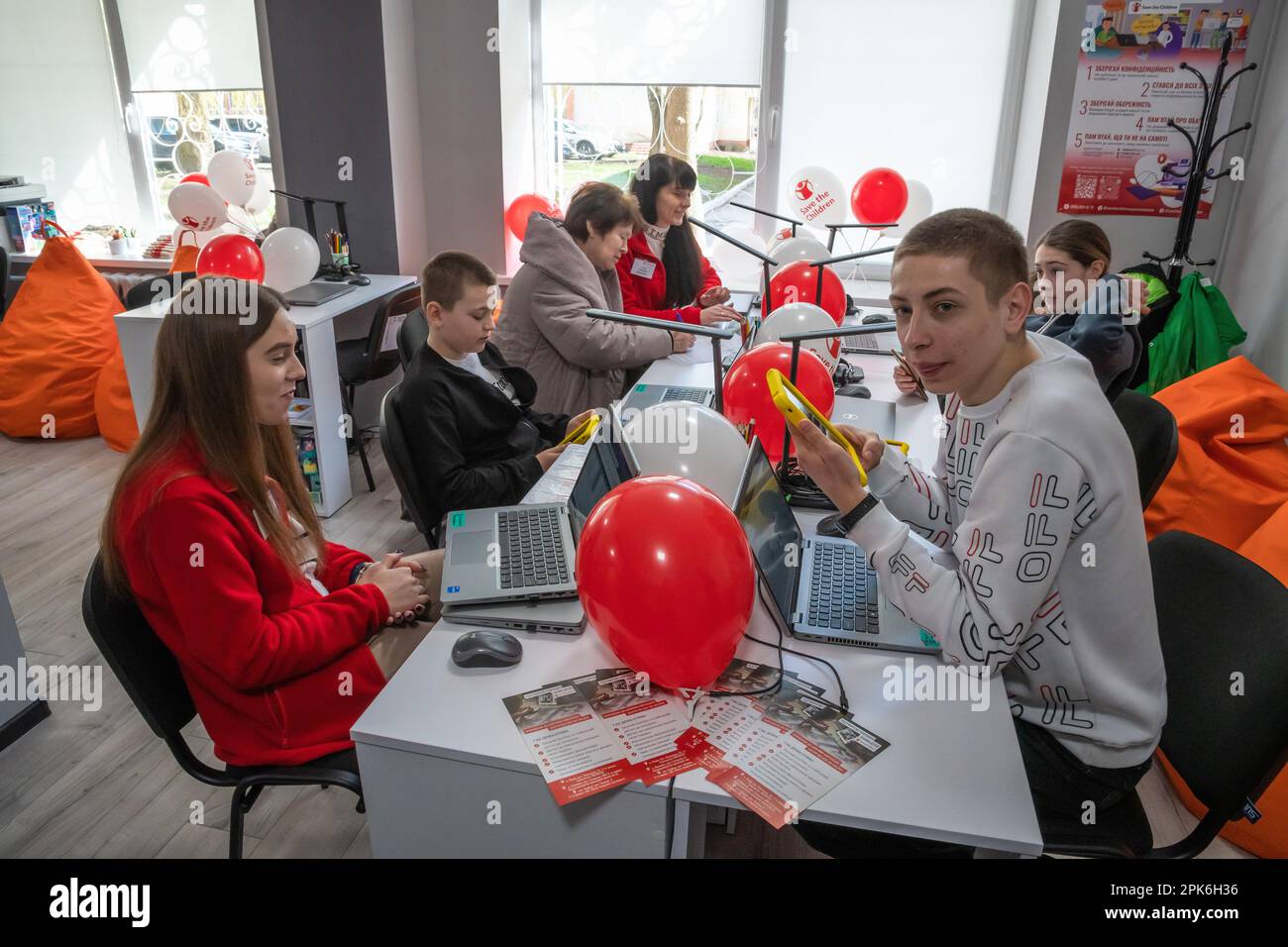 Children sit at a table with laptops and tablets in a classroom ...
