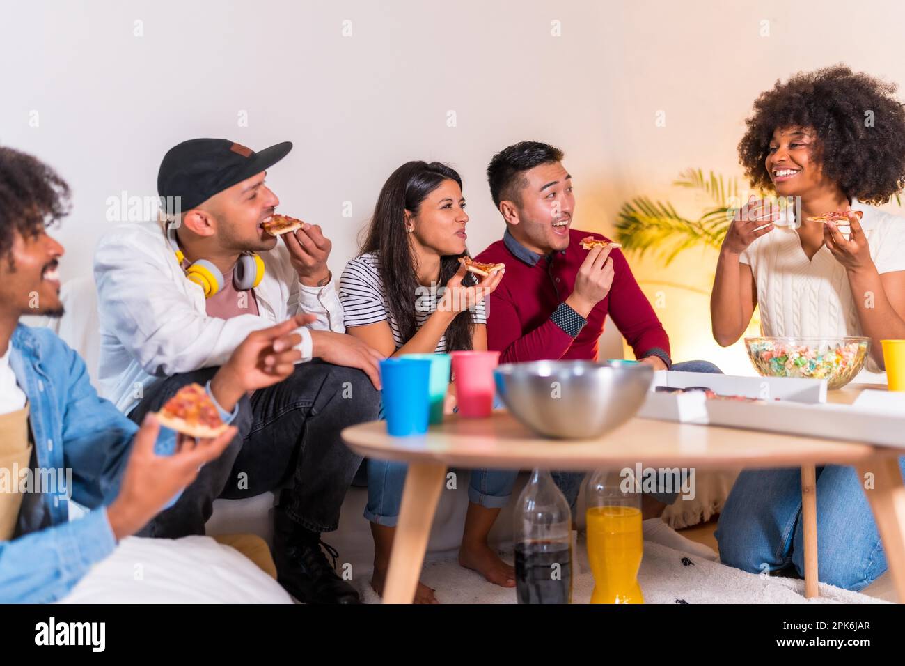 Group of multiethnic friends on a sofa eating pizza and drinking soda ...