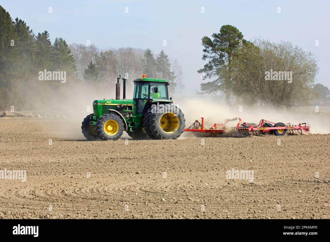 John Deere tractor pulling harrows, harrow field with windblown dust ...