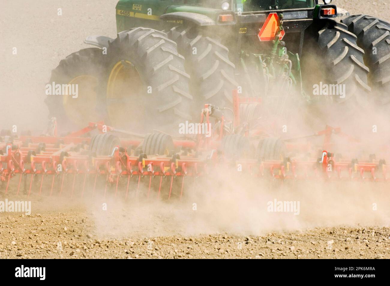 Close-up of tractor pulling harrows, harrow field with windblown dust ...