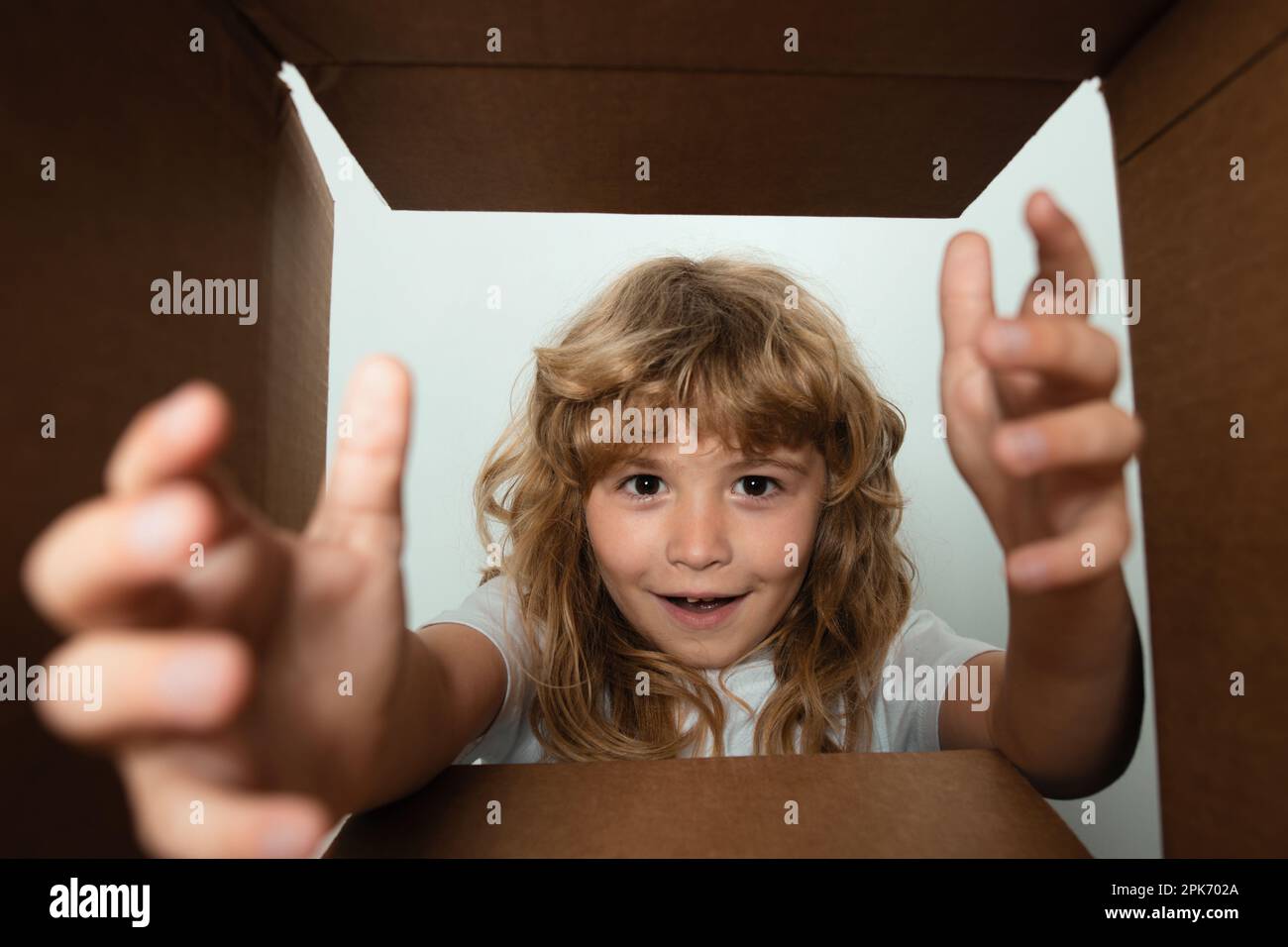 Child opens carton box and pulling out gift from it. Small boy looking ...