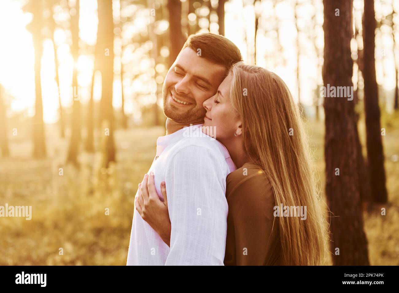 Illuminated by sunlight. Happy couple is outdoors in the forest at ...