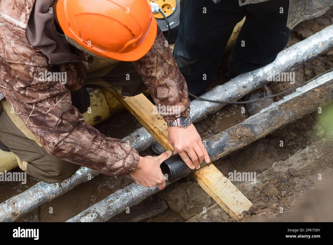 Worker in helmet repairs communal water pipe in trench on street. Work ...
