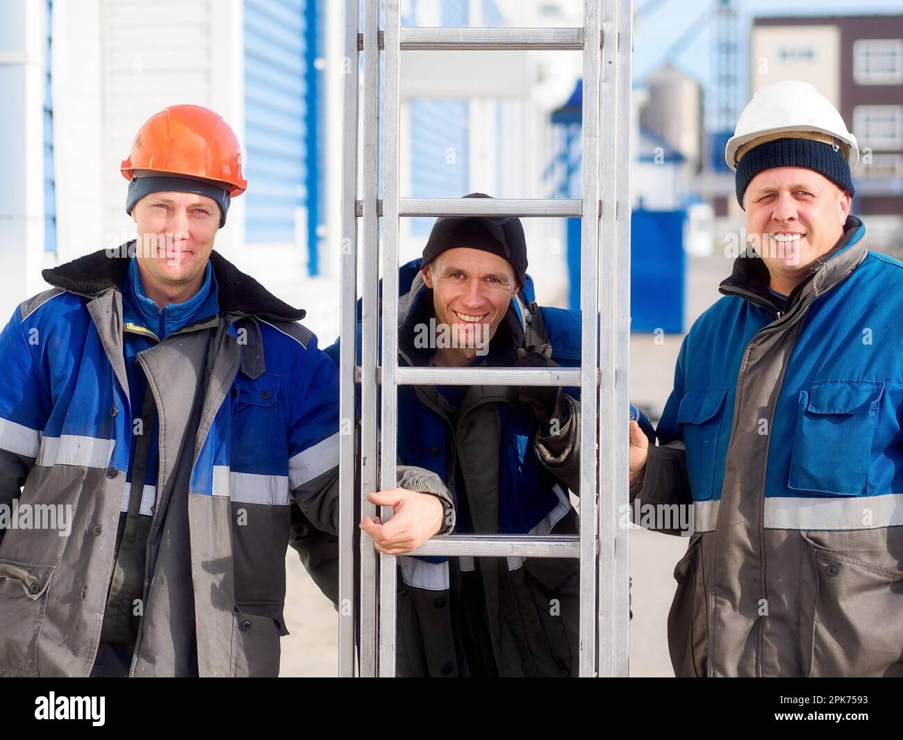 Three workers in winter overalls and helmets stand outside looking at ...