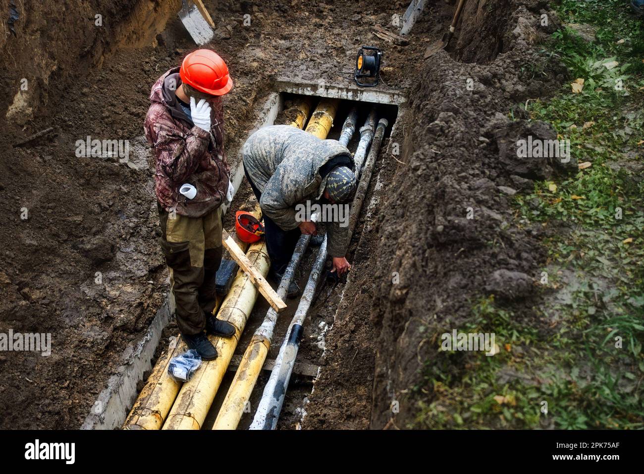 Two workers change public water pipes in trench on rainy autumn day ...