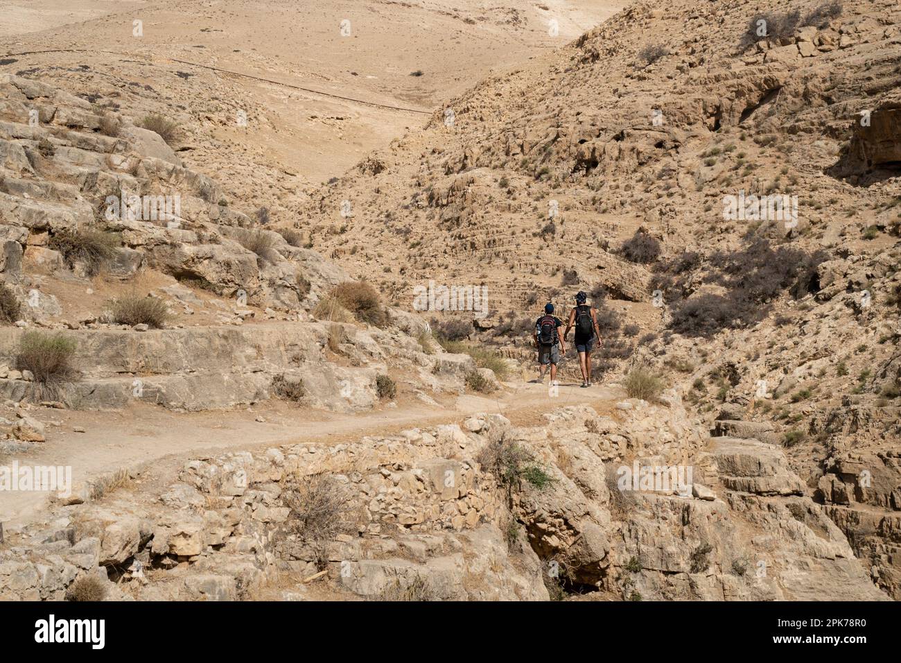 Two men hiking on a path in the arid Judea desert, Israel, on a hot day ...