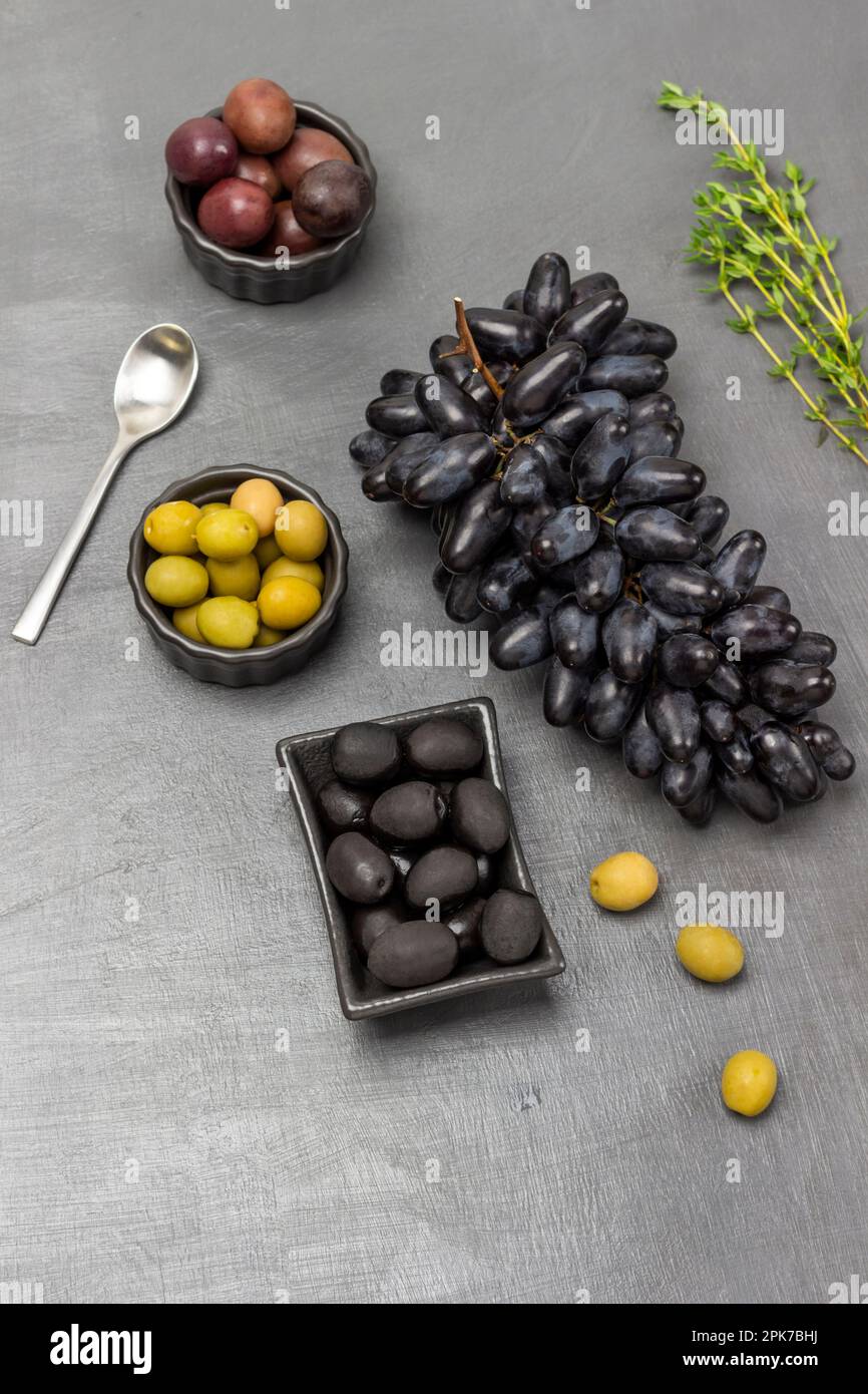 Olives in bowls. Bunch of black grapes, sprig of thyme and spoon on ...
