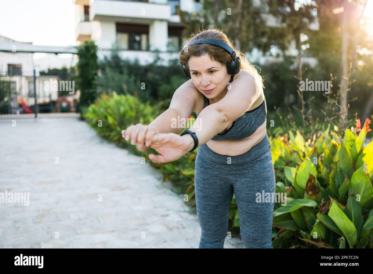 Adorable fat woman in tracksuit is engaged in fitness outdoor side view ...