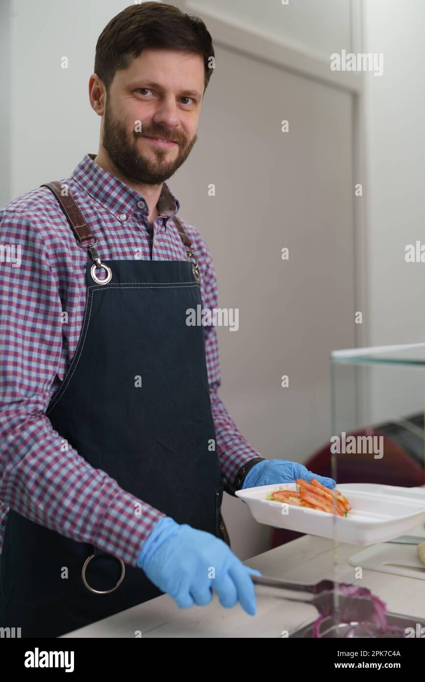 Portrait of a cheerful white man cooking Greek kalamaki dish in a fast ...