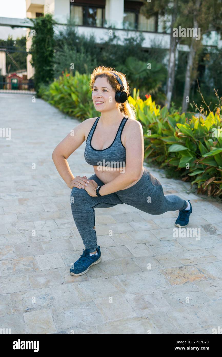 Adorable fat woman in tracksuit is engaged in fitness outdoor side view ...