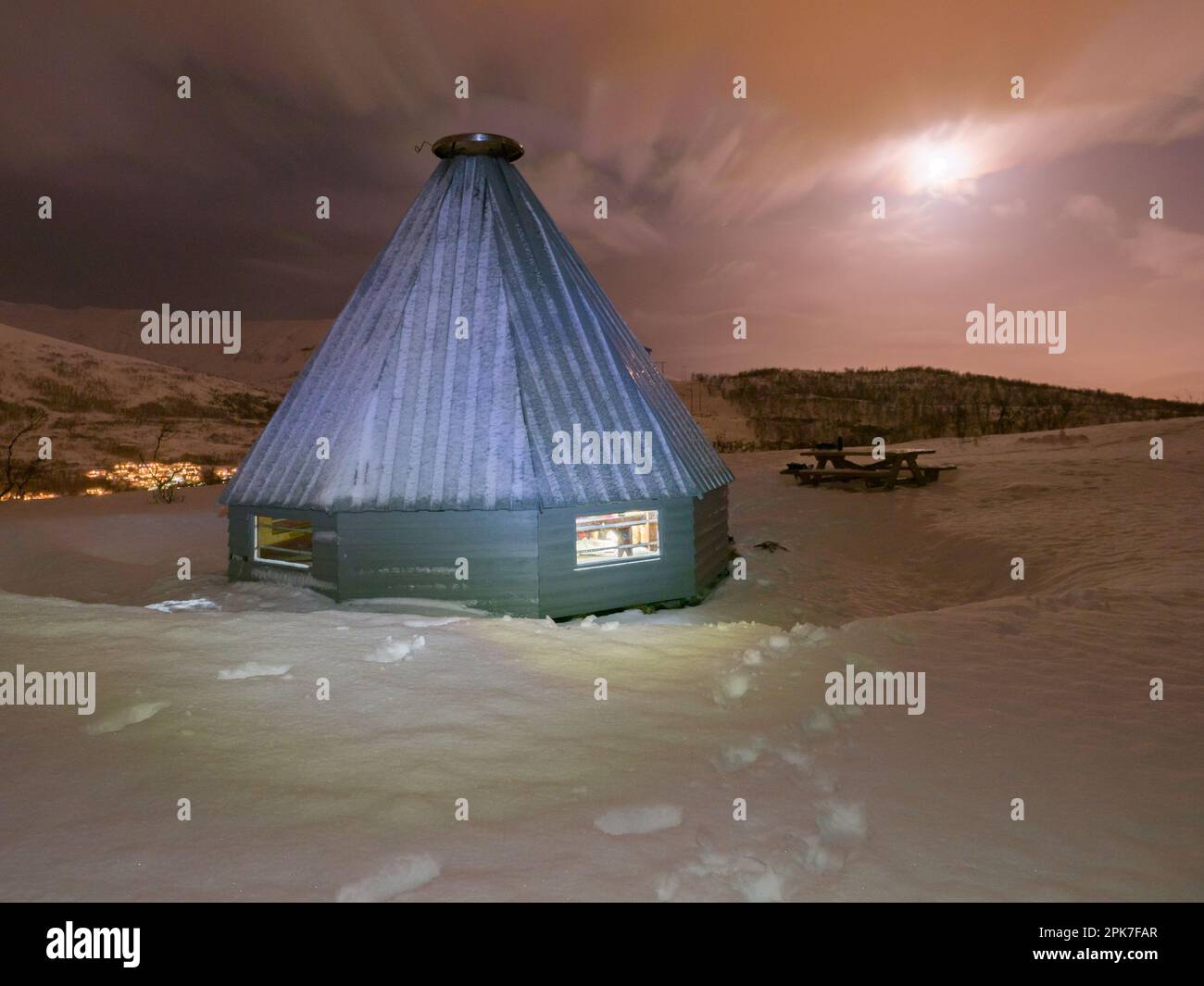 Wooden cabin in Northern Norway in winter. Visible lights inside. Gate ...