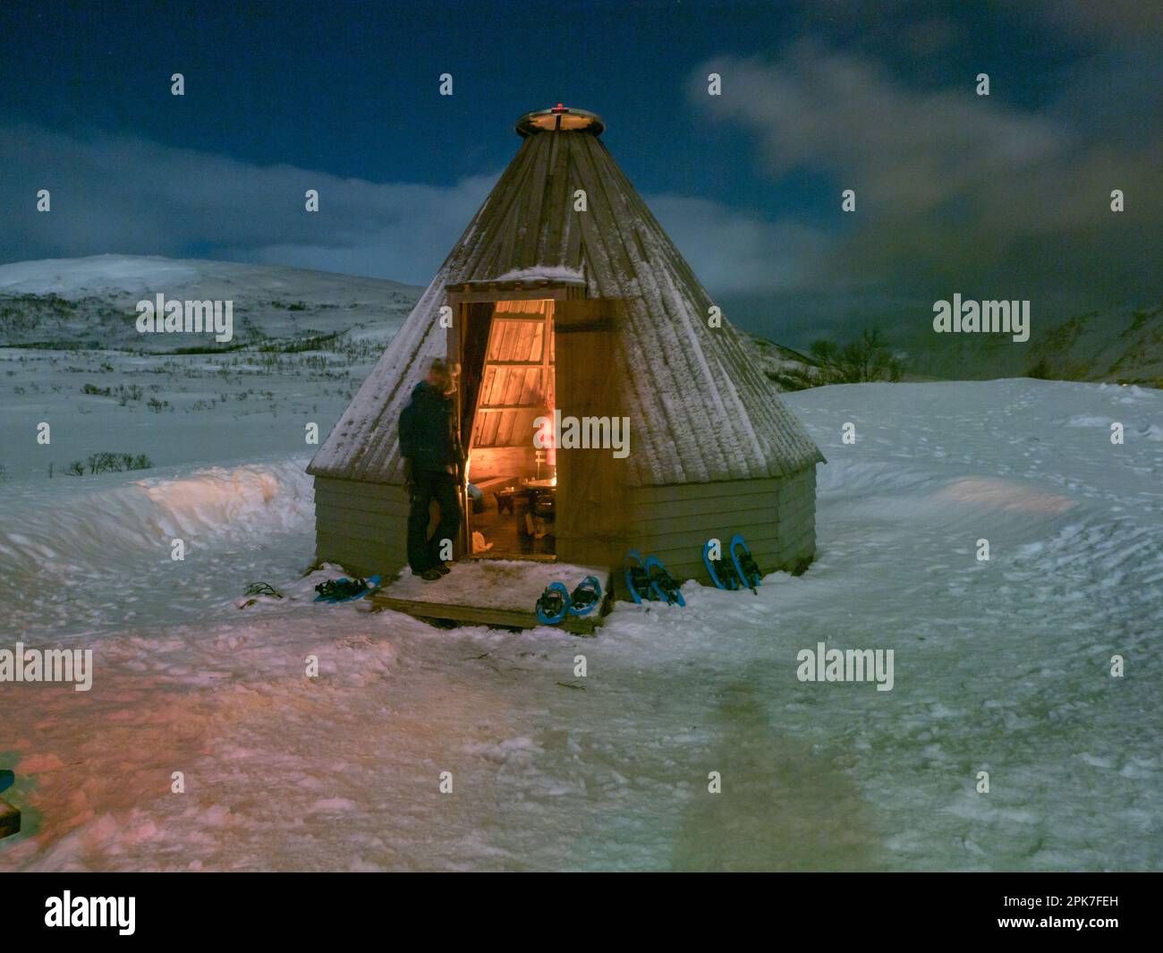 Wooden cabin in Northern Norway in winter. Visible lights inside. Gate ...