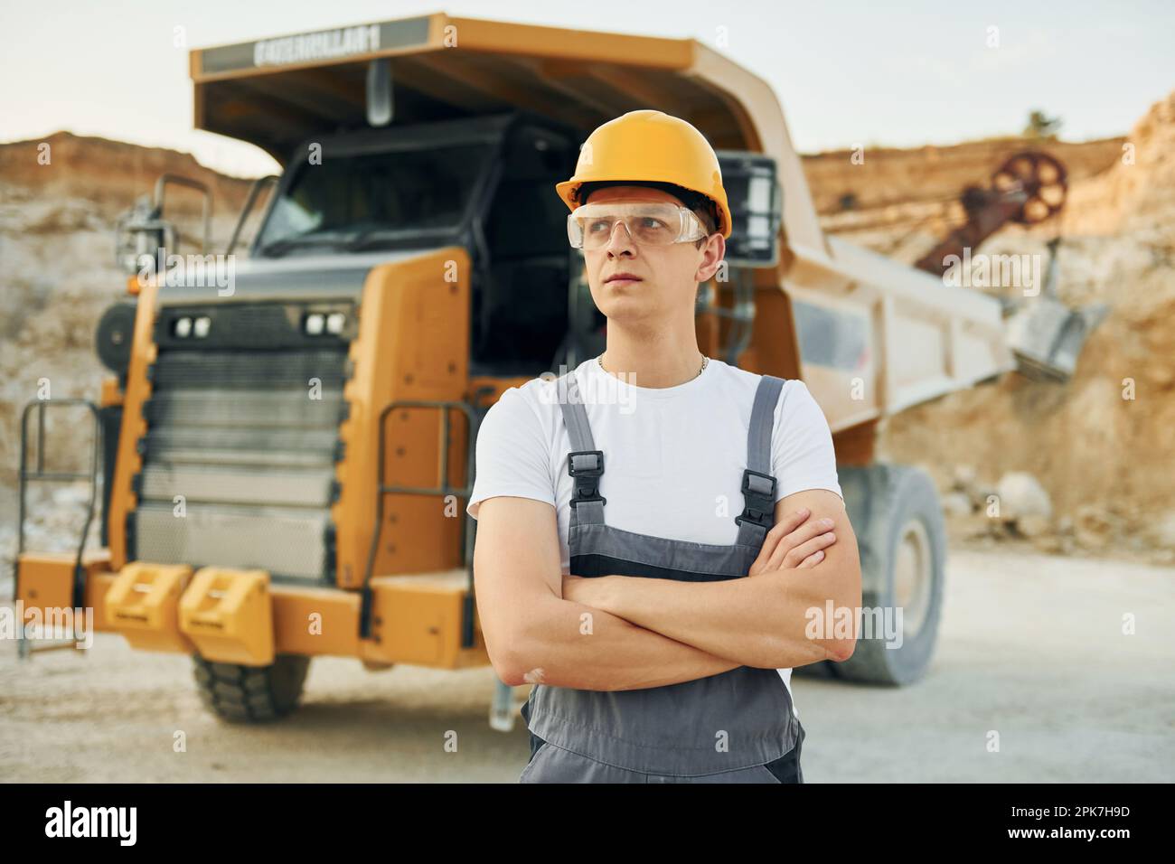 Standing in the front of vehicle. Worker in professional uniform is on the borrow pit at daytime ...
