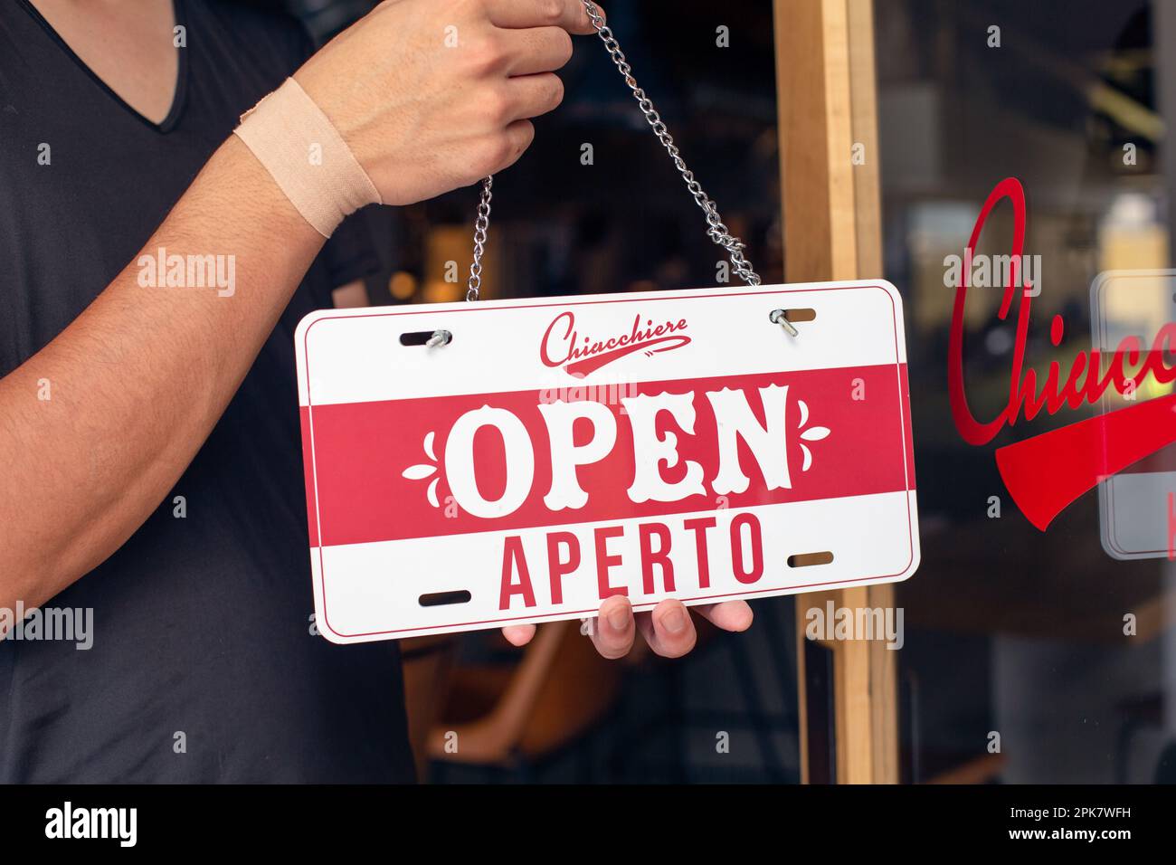 Man hanging up an Open sign on a restaurant door. Dual language ...