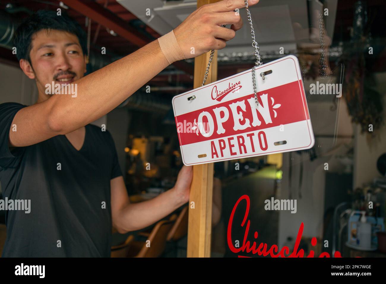 Man hanging up an Open sign on a restaurant door. Dual language ...