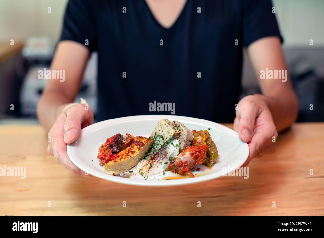 A man standing at a restaurant counter presenting plates of cooked food ...