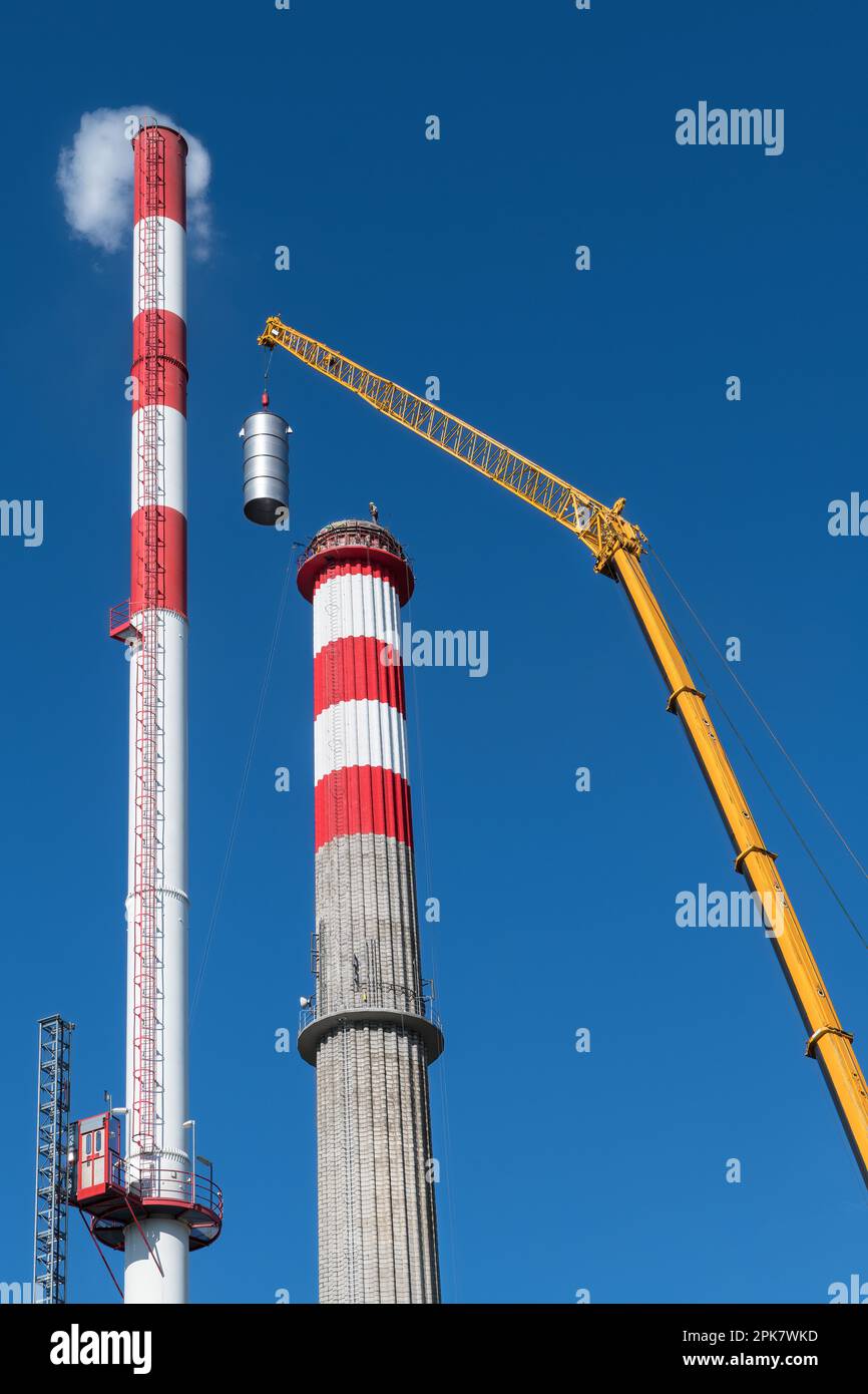 Tall smoking and renewing factory chimney with crane boom on blue sky ...