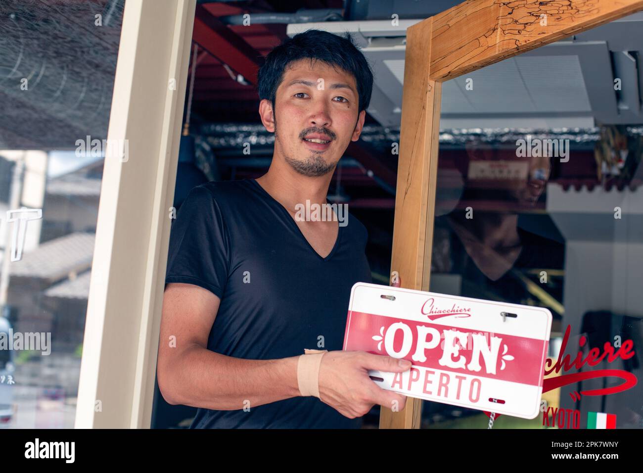 Man hanging up an Open sign on a restaurant door. Dual language ...