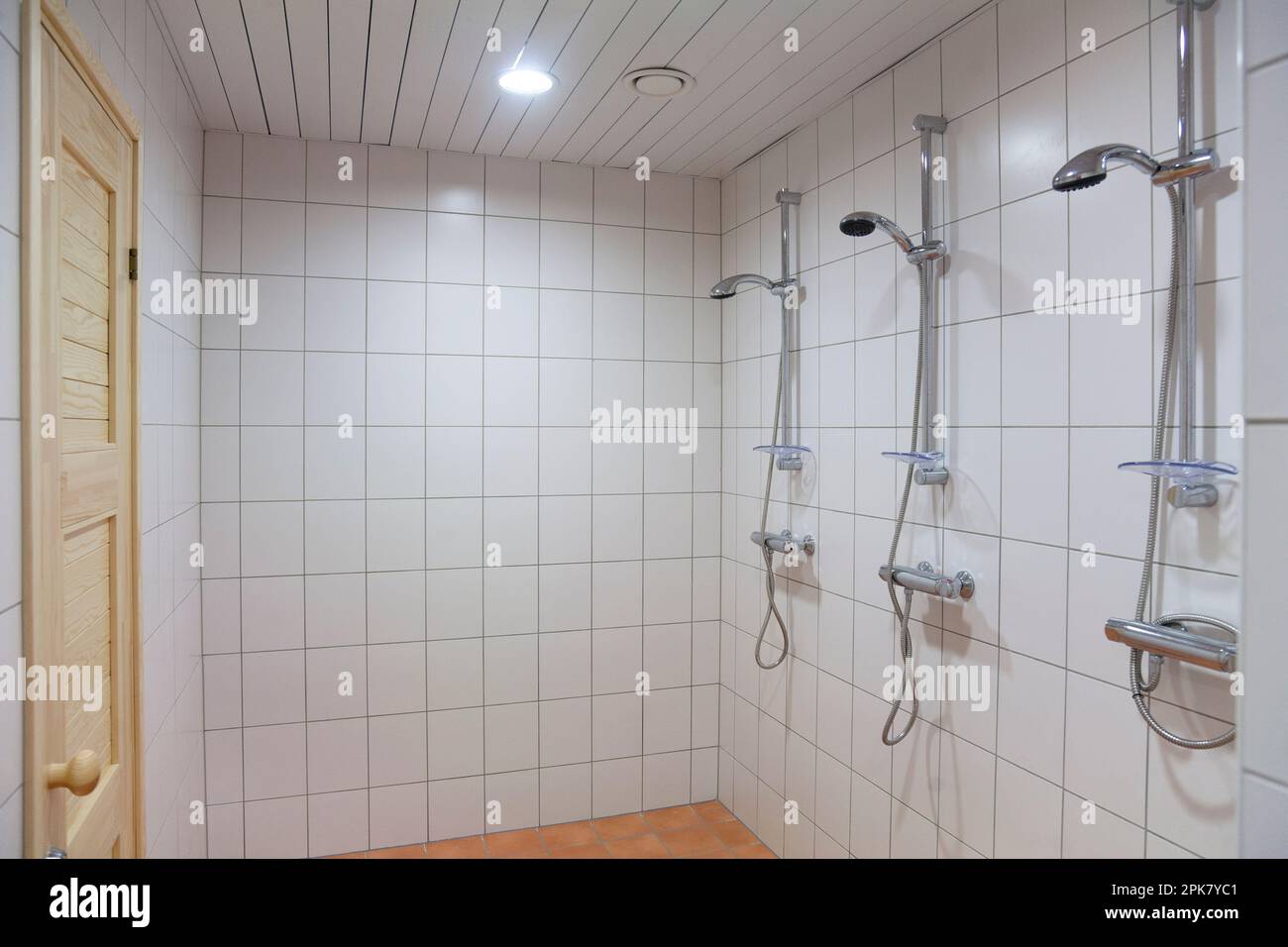 A large shower room, tiled in white tiles,with three showers. Changing ...