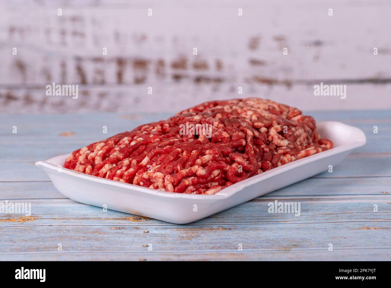 Raw ground beef in a white polystyrene tray on a wood background. Fresh ...