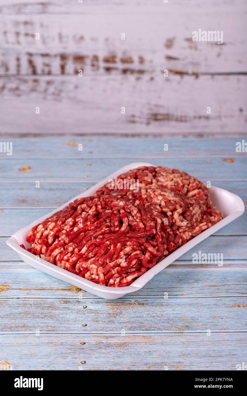 Raw ground beef in a white polystyrene tray on a wood background. Fresh ...