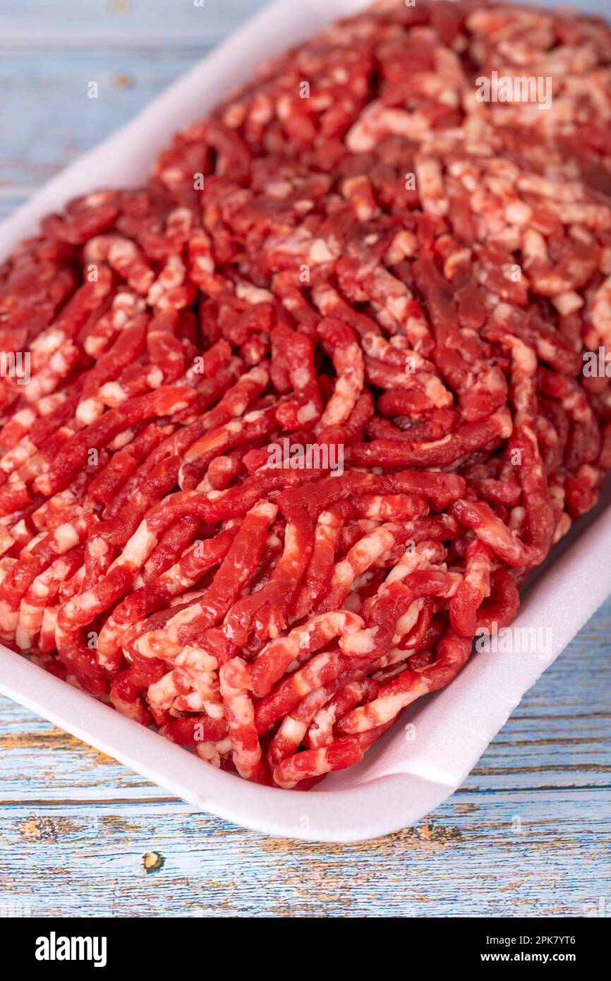 Raw ground beef in a white polystyrene tray on a wood background. Fresh ...