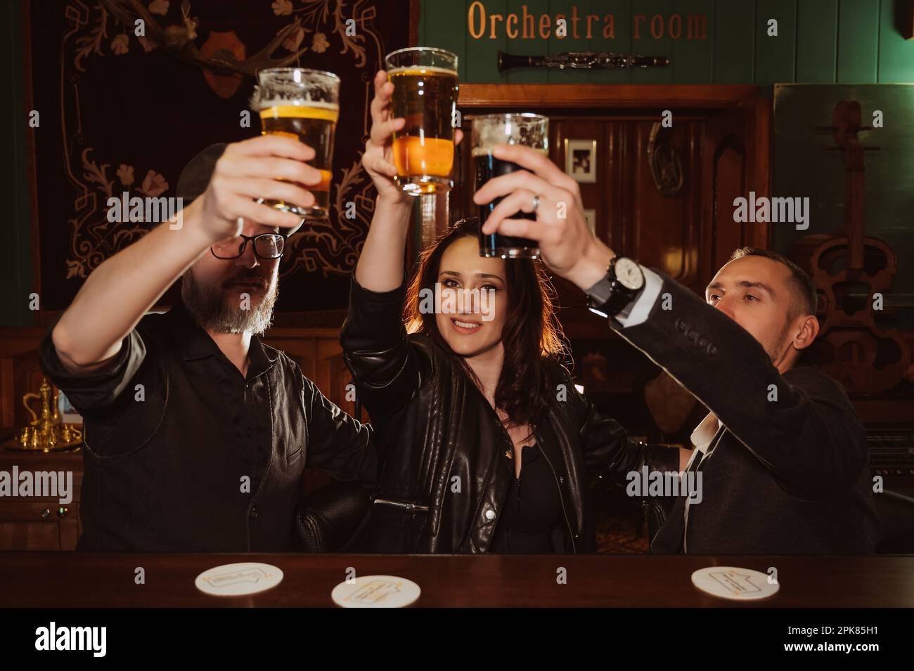 three happy friends happily clink glasses with beer behind bar counter ...