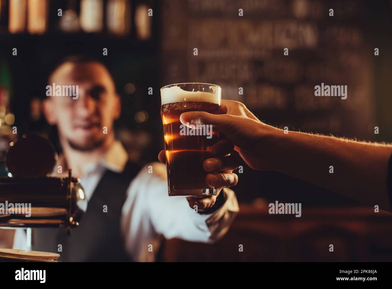 bartender serves a glass of light draft beer to a male guest at bar ...