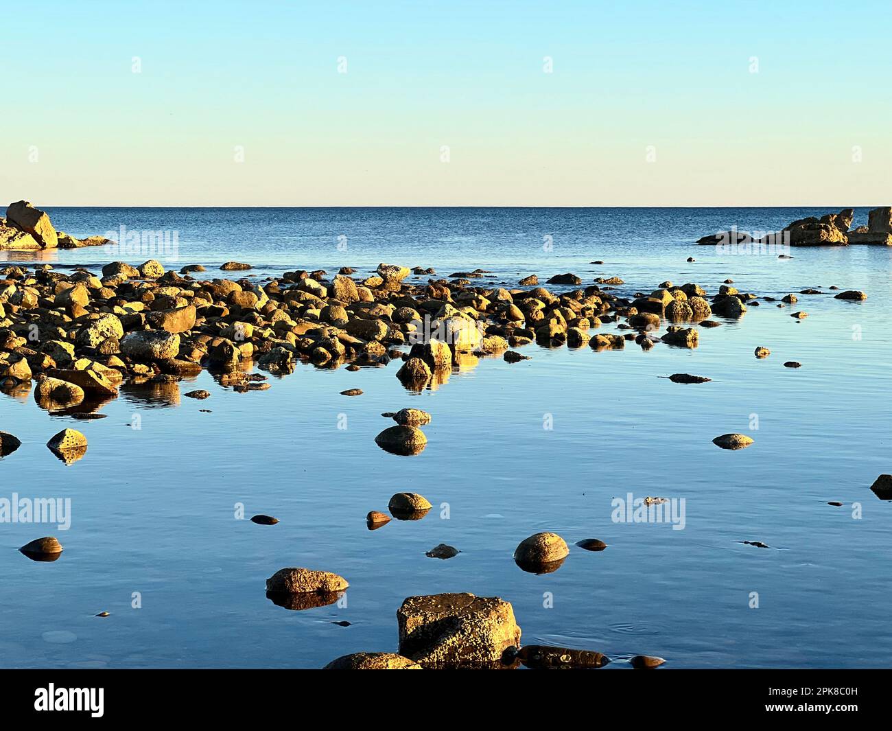 The photo depicts a group of dark grey rocks rising from the calm ...