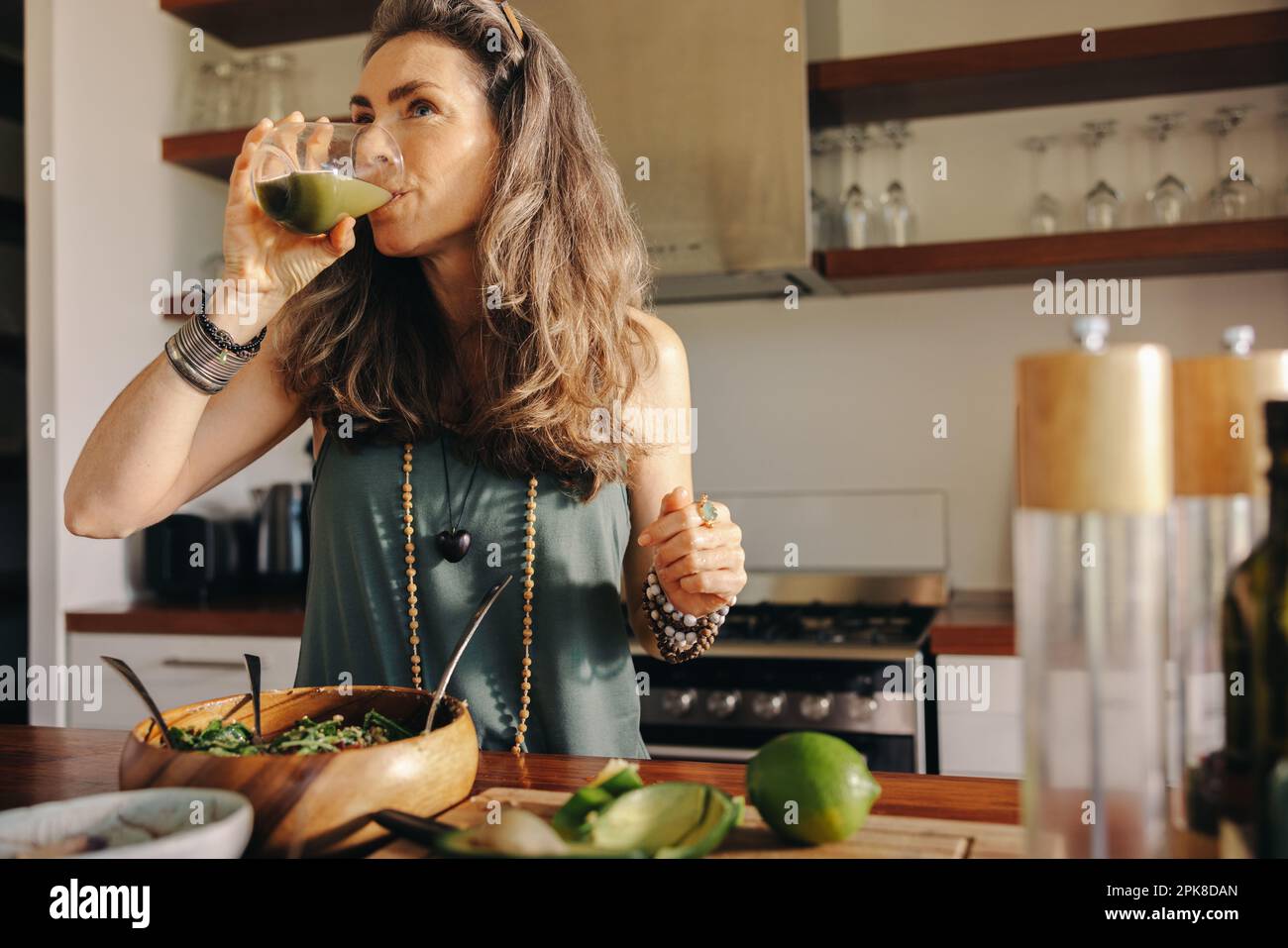 Vegan woman drinking some green juice while having a buddha bowl ...