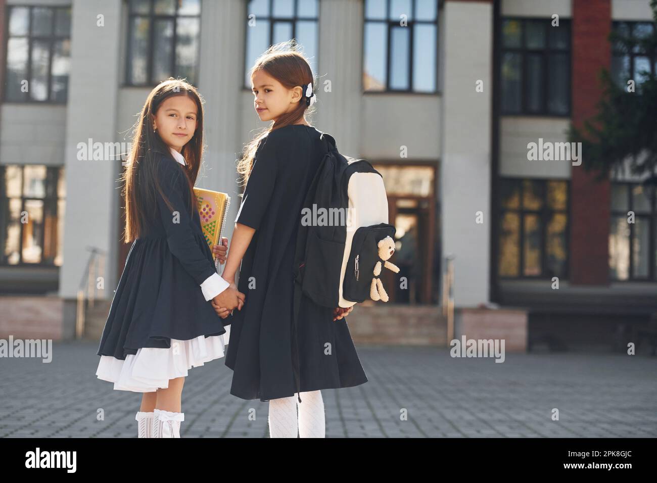 Walking together. Two schoolgirls is outside near school building Stock ...