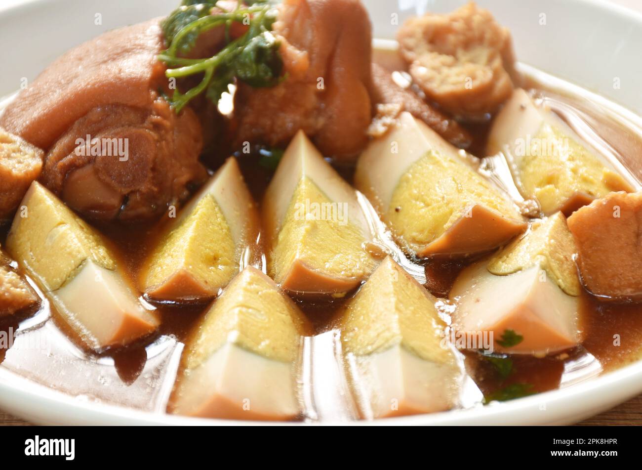boiled half cut egg with tofu in herb brown soup and pork leg on plate ...