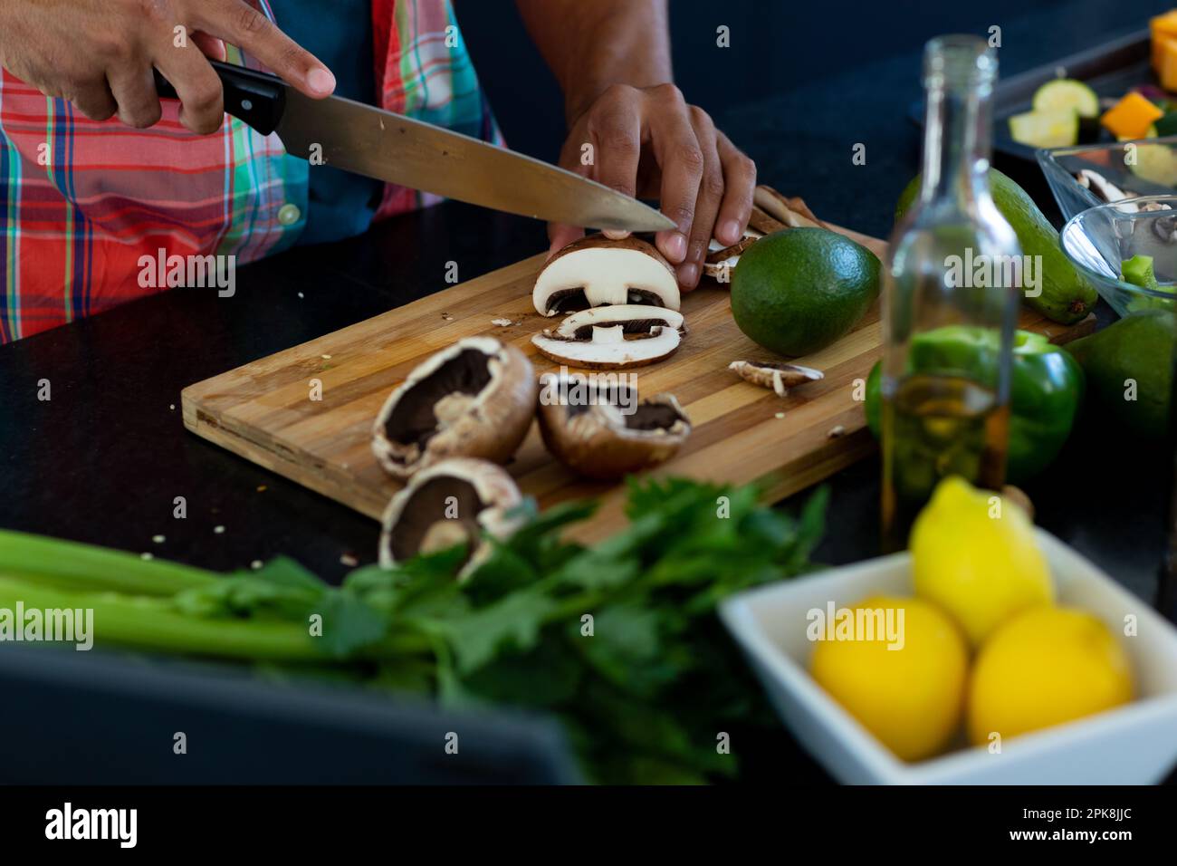 Close up of hands of biracial man preparing dinner, chopping mushrooms ...